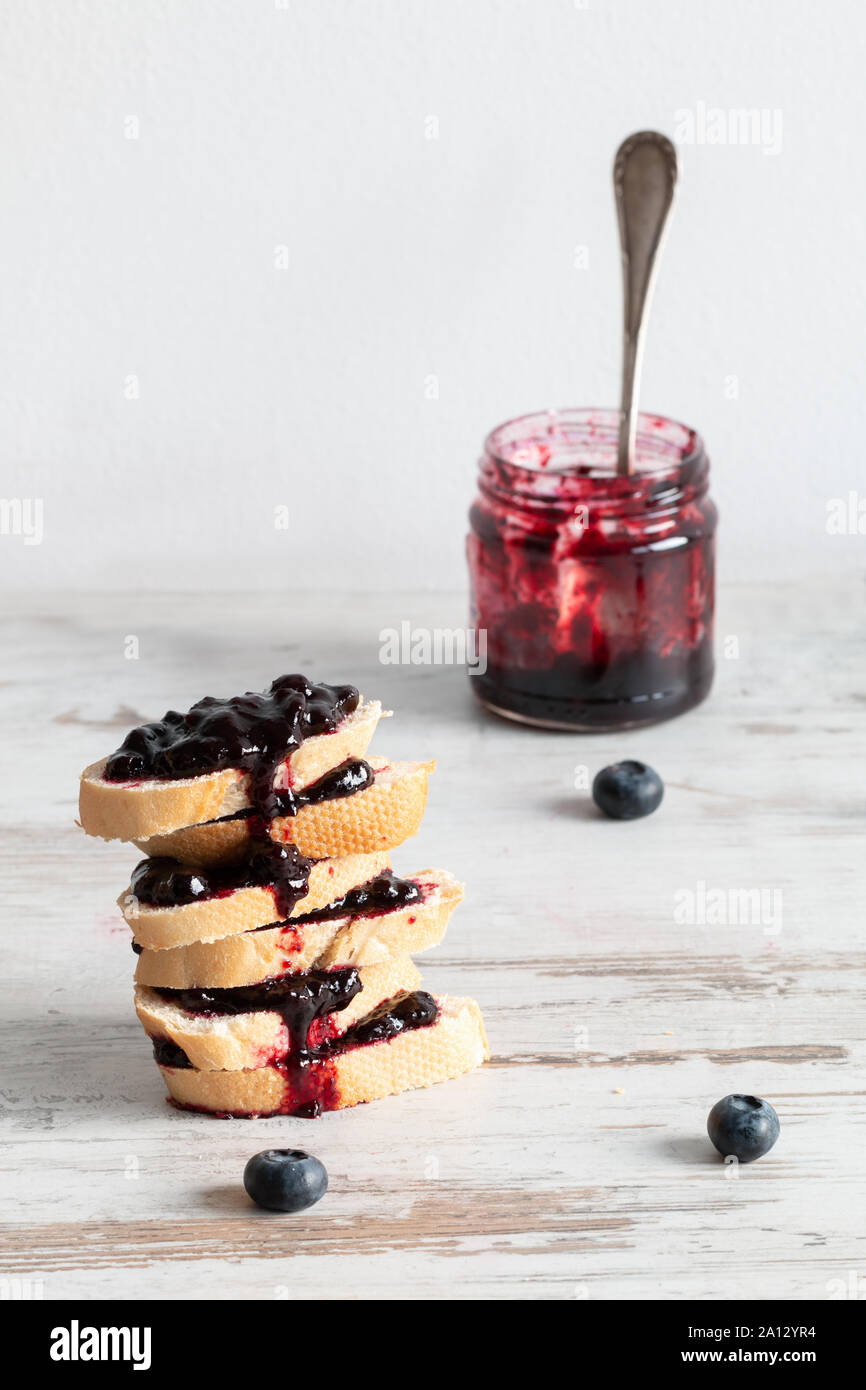 A pile of bread smeared with blueberry jam. Next to blueberry jam in a ...