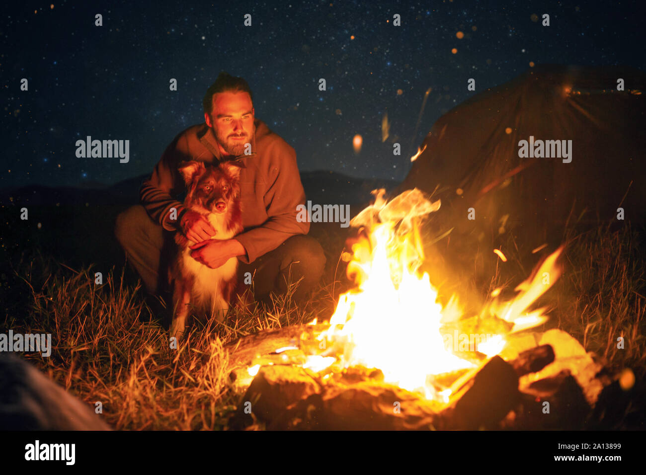 A man and his dog next to a campfire at night Stock Photo - Alamy