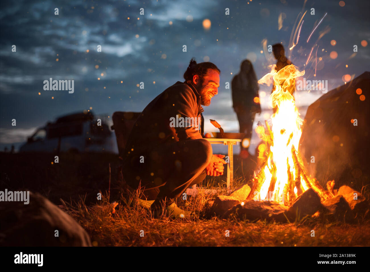 Smiling man next to a bonfire in the dark Stock Photo - Alamy