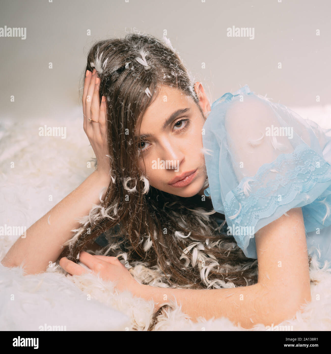 Young female among fluffy white feathers, pillow fight. Drowsy brunette ...