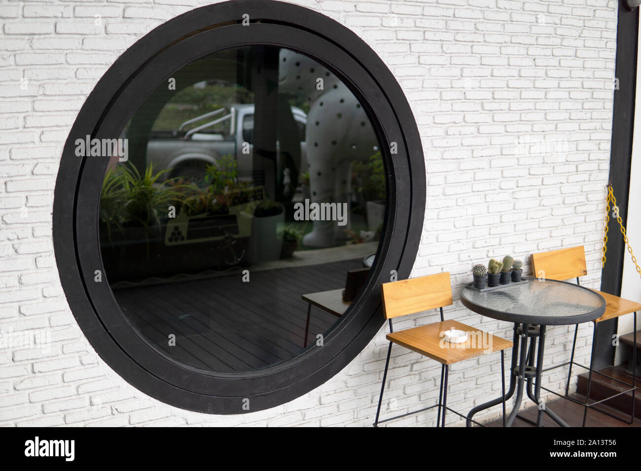 Circular window view on a white brick wall with cafe table and chair ...