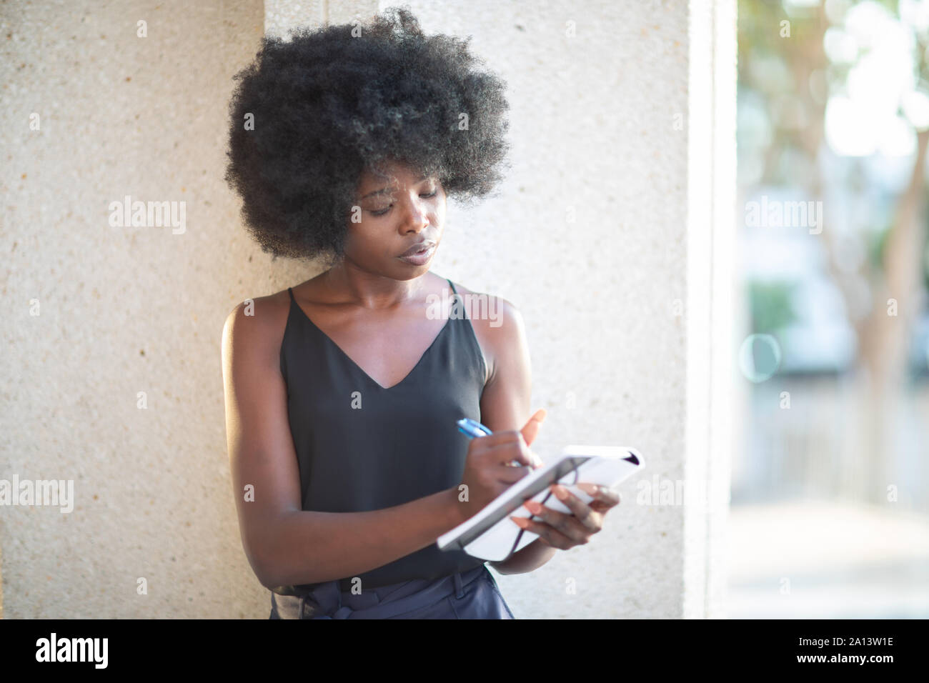 African American lady writing notes leaning on a wall of a concrete ...