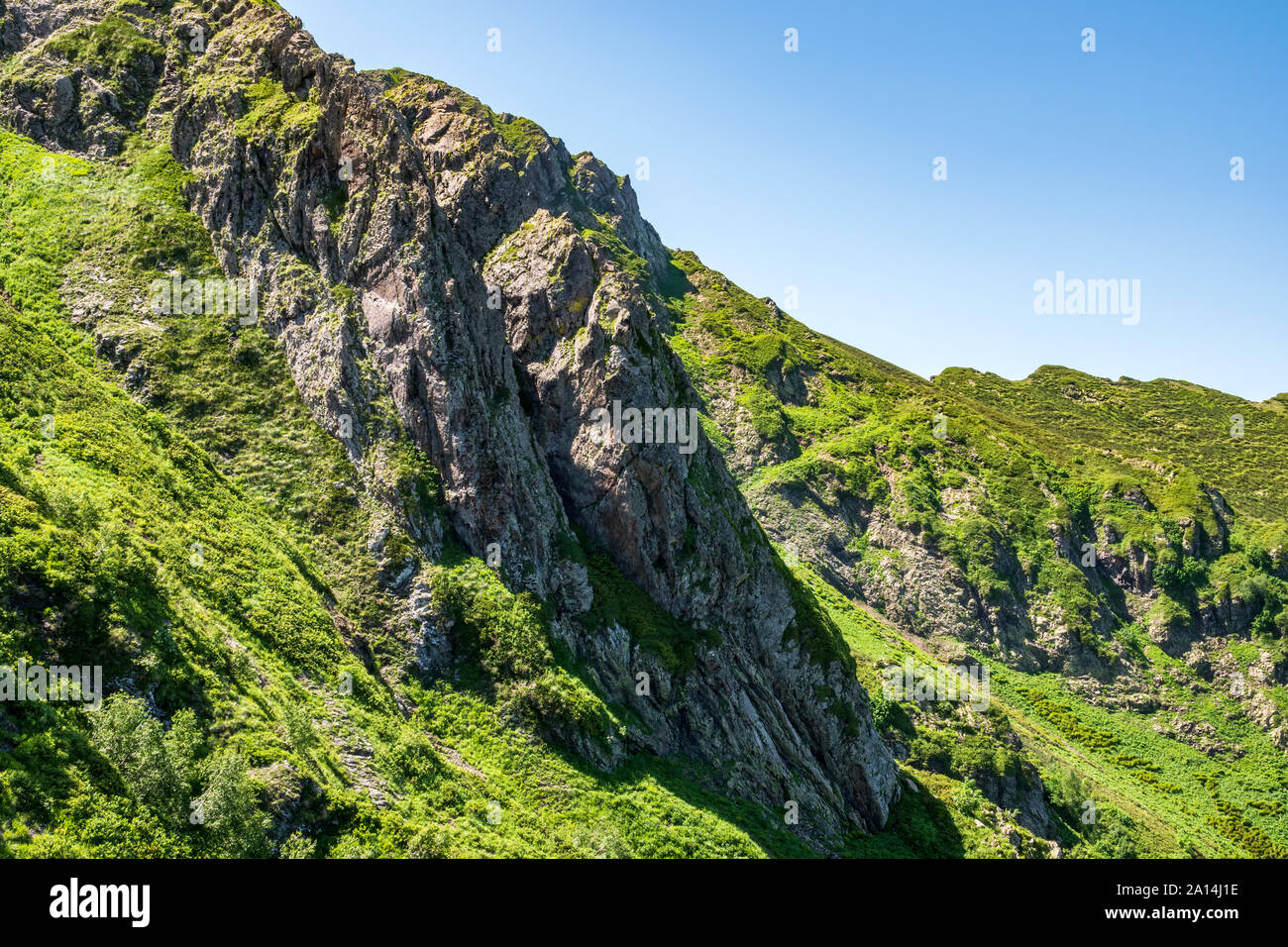 A rocky mountain peak with growing grass is lit by the rays of the sun ...