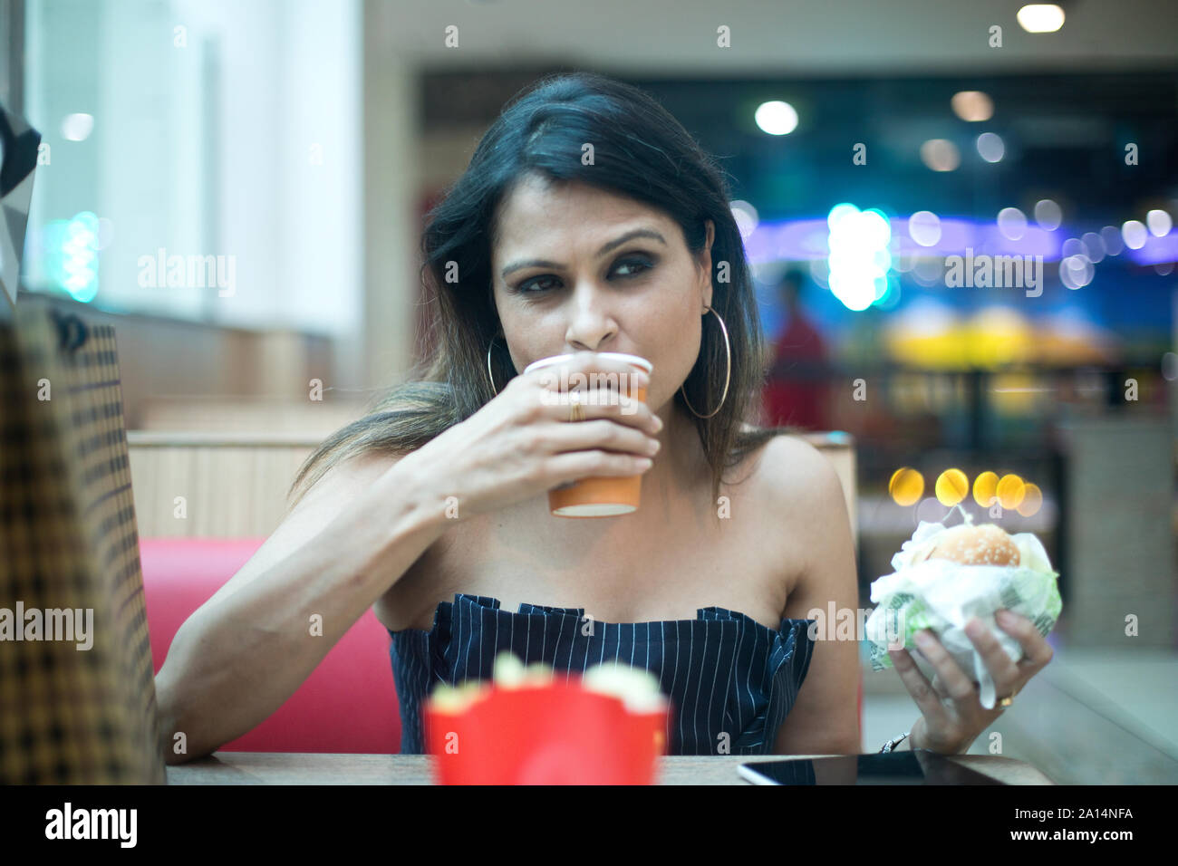 Fashionable woman drinking coffee and eating burger after shopping at ...