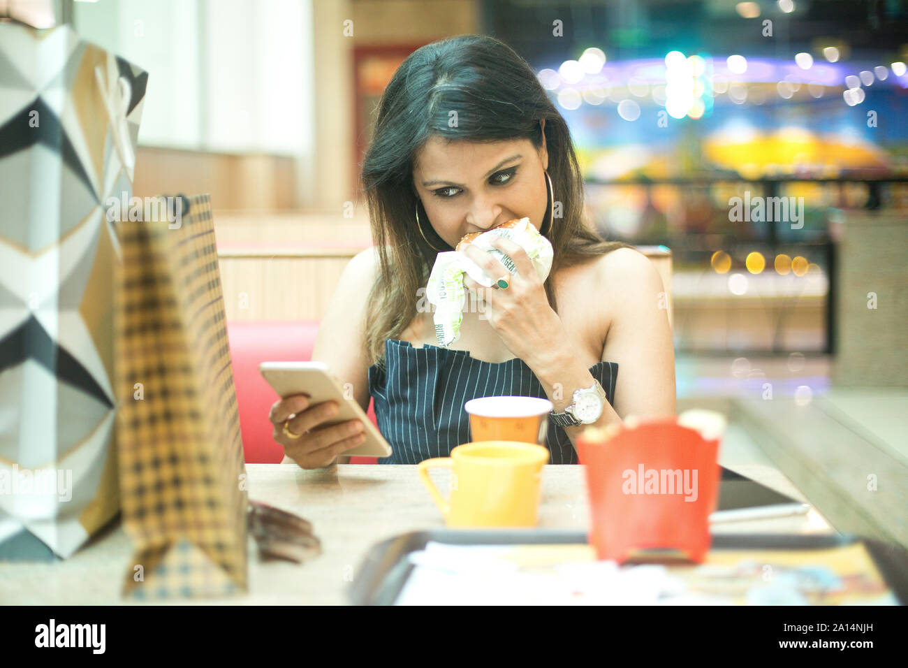 Fashionable woman drinking coffee and eating burger after shopping at ...