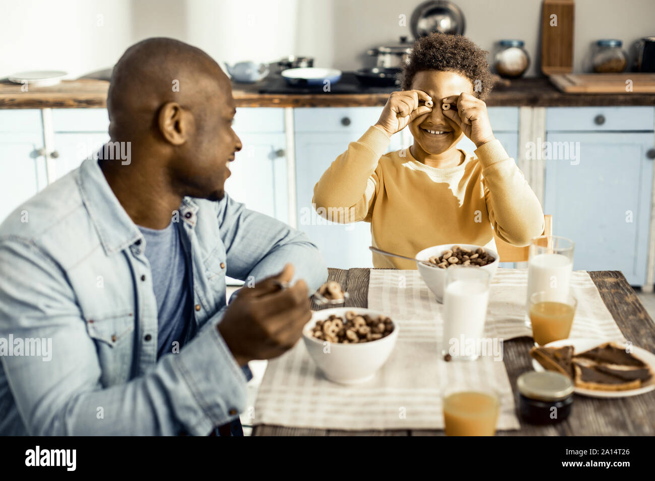 Smiling dad watching frisky boy playing with cereal Stock Photo - Alamy