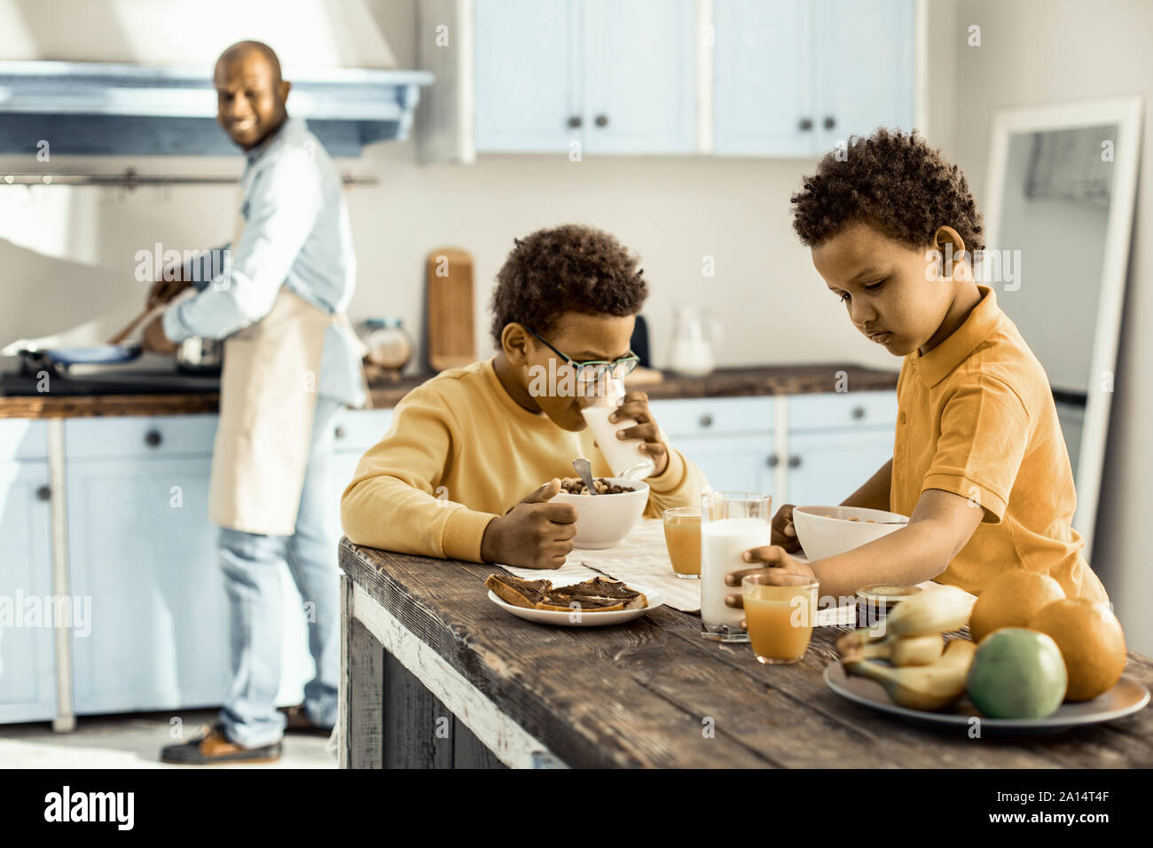 Dad cooking dessert while two kids enjoying main meal at the table ...