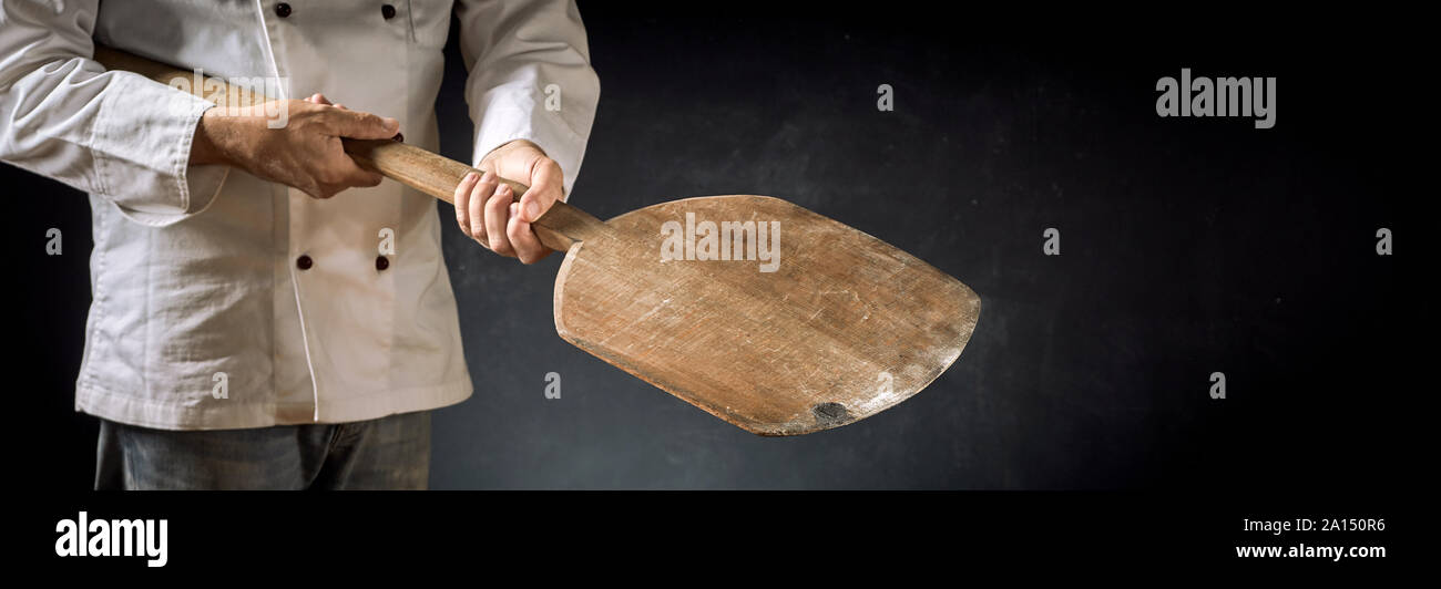 Cook or chef in a pizzeria holding an empty wooden paddle in a close up ...