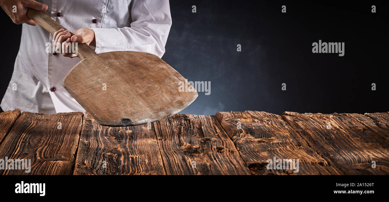 Chef holding an empty wooden pizza paddle over an old rustic kitchen ...