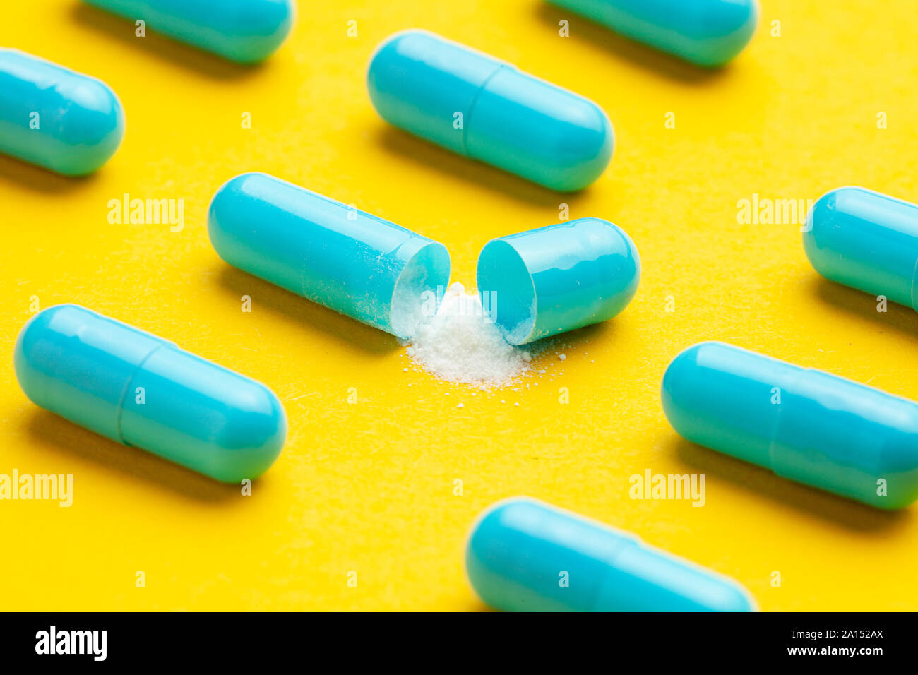 Blue tablets in capsules. One capsule is open. Yellow background Stock ...