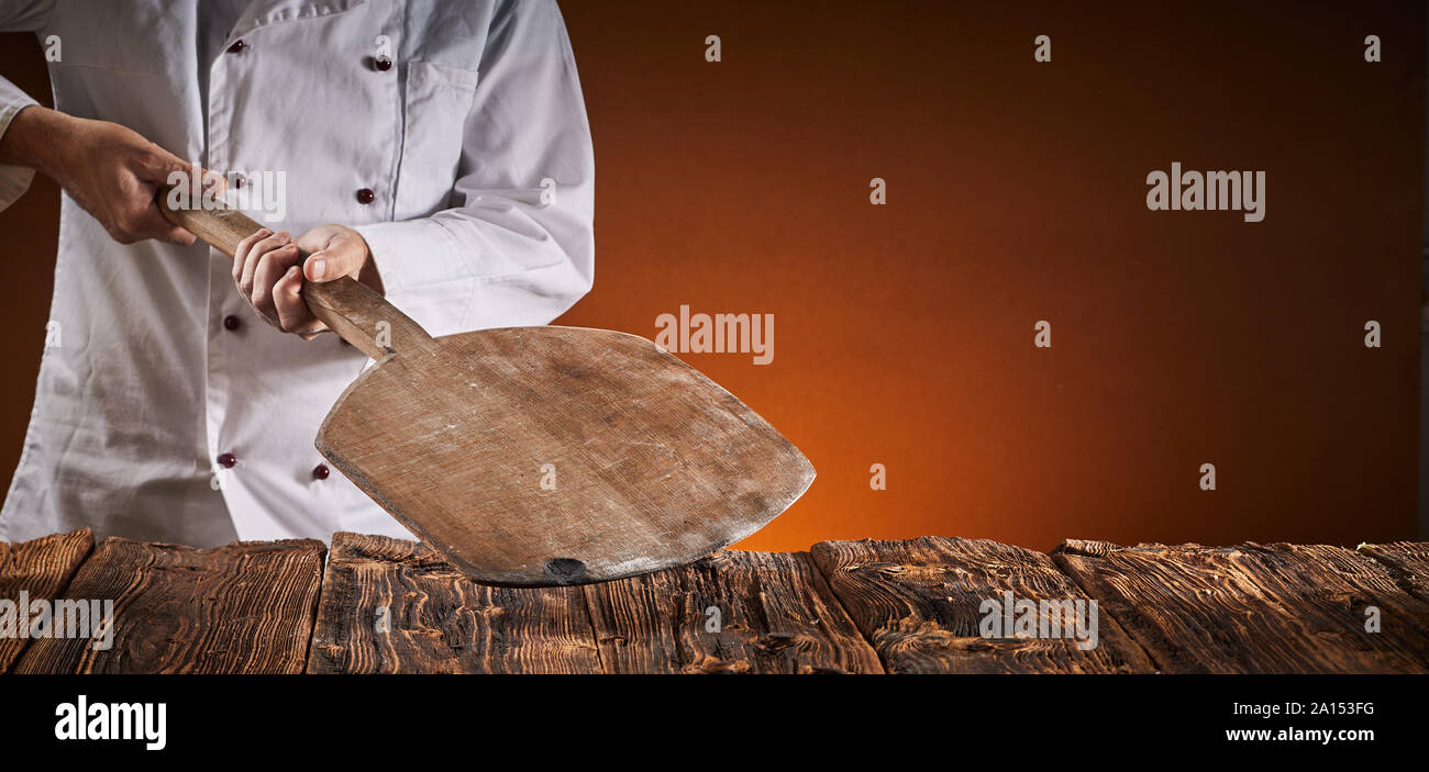 Restaurant chef in a pizzeria holding a wooden paddle over a rustic ...