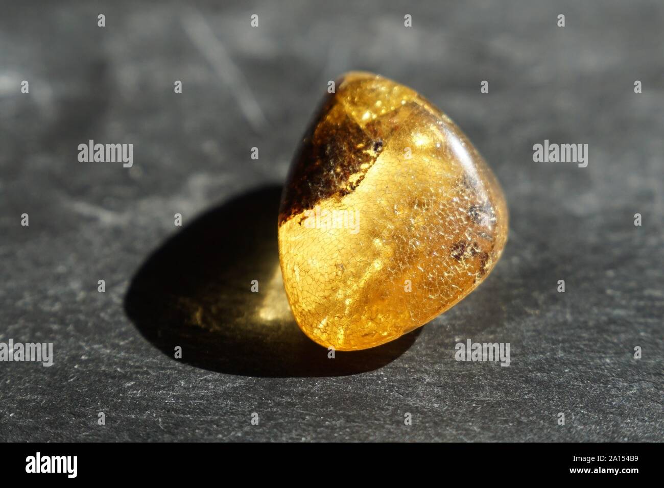 Amber stone with cracked surface, on gray slate background, lit by the ...