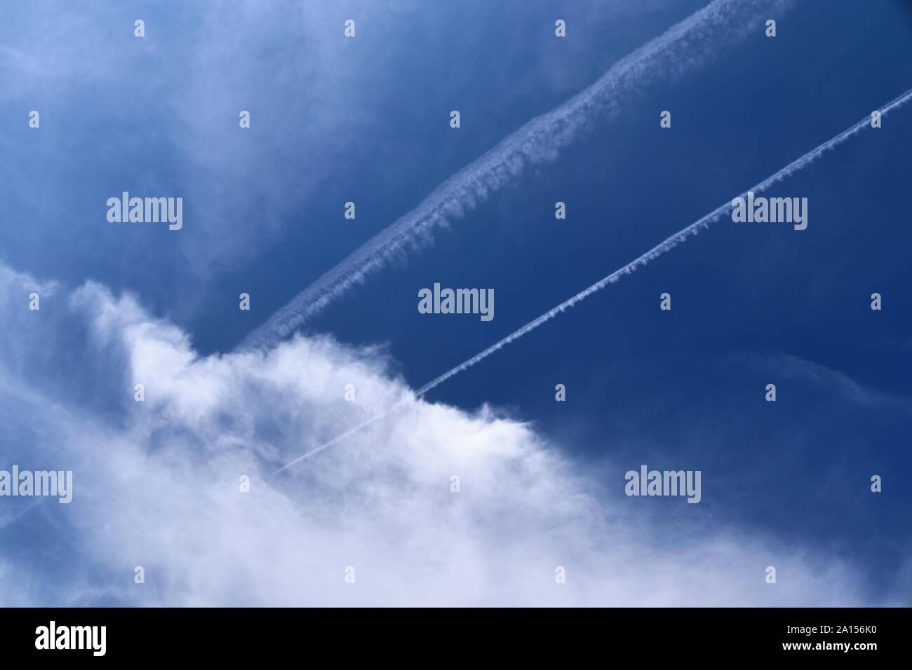 Aircraft condensation contrails in the blue sky inbetween some clouds ...