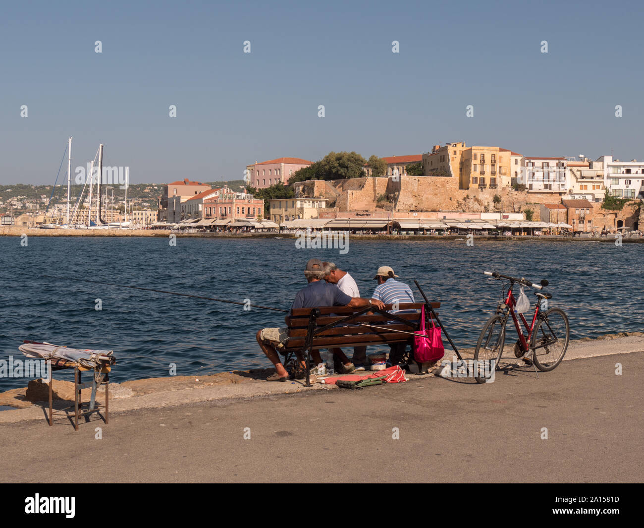 Three people sitting on a bench in the harbour in Chania, Crete Stock ...