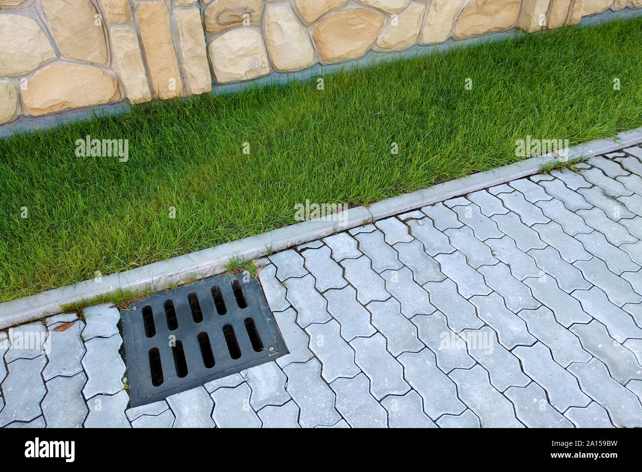 Plastic drain gutter, green grass lawn and stone pavement sidewalk ...