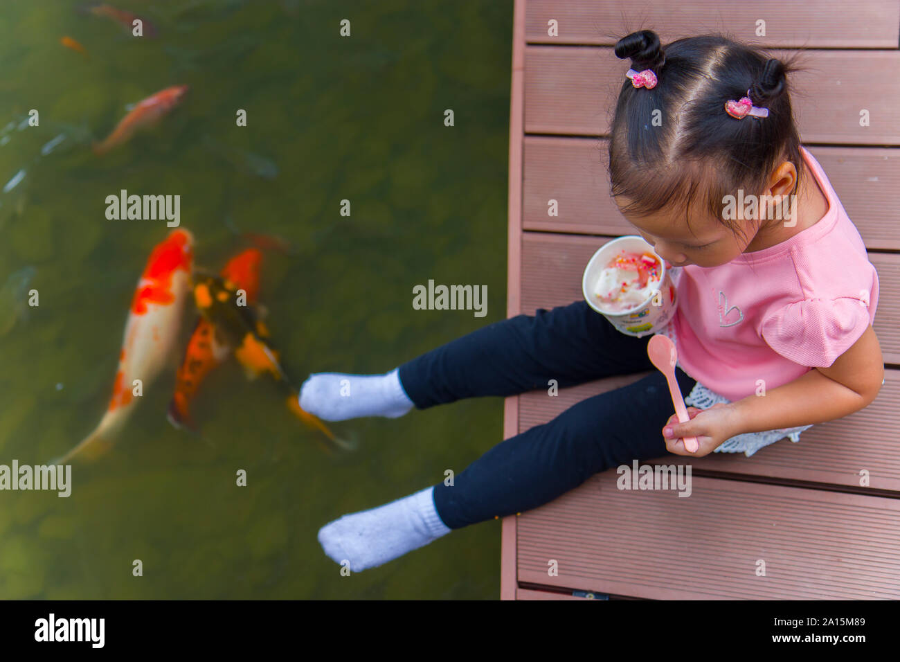 Little kids look at the water and feeding fishs on the wooden bridge ...