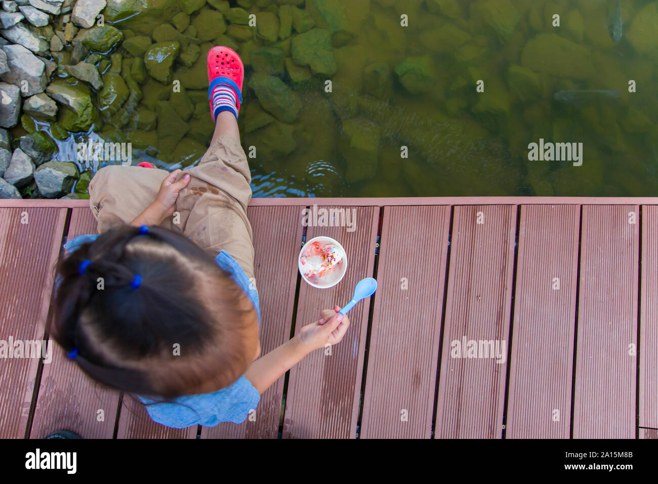 Little kids look at the water and feeding fishs on the wooden bridge ...