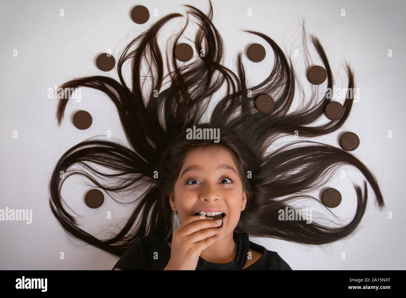 Close up of smiling girl lying on floor eating biscuit with her hair ...