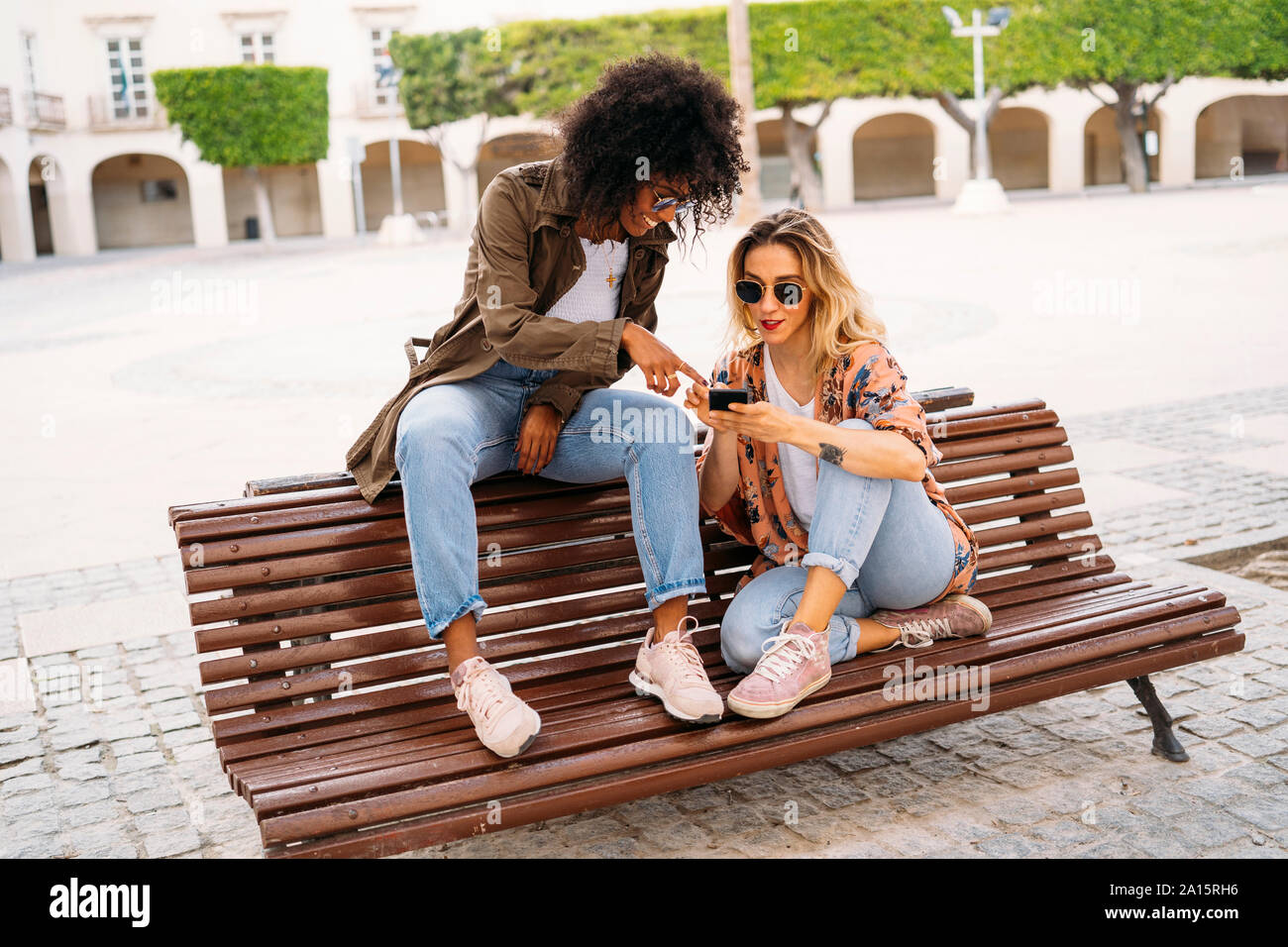 Multicultural happy women talking and using smartphone, sitting on ...