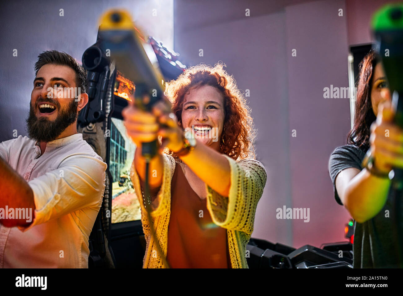 Happy friends playing and shooting with pistols in an amusement arcade ...