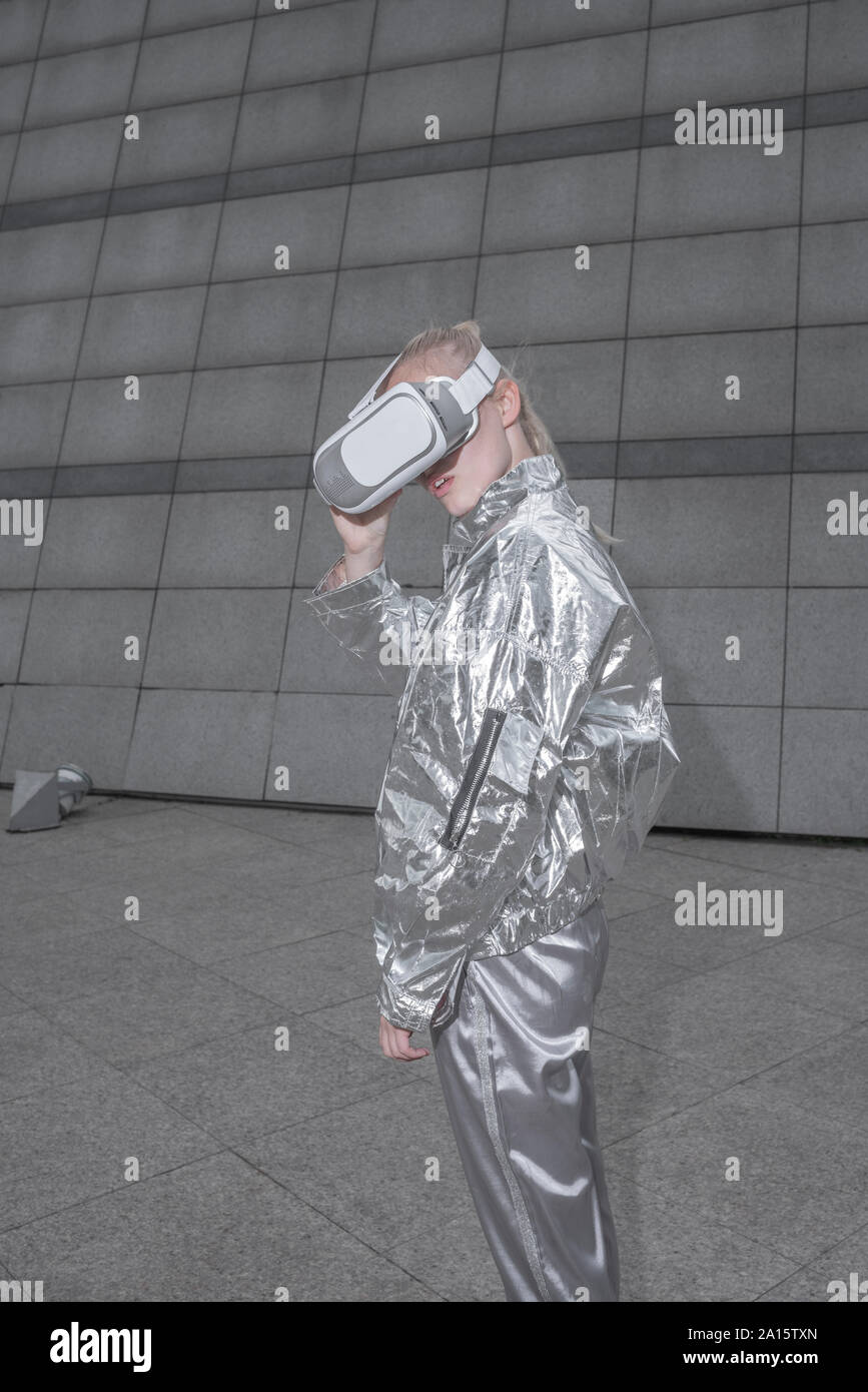 Girl in silver suit. looking through VR goggles in futuristic city ...