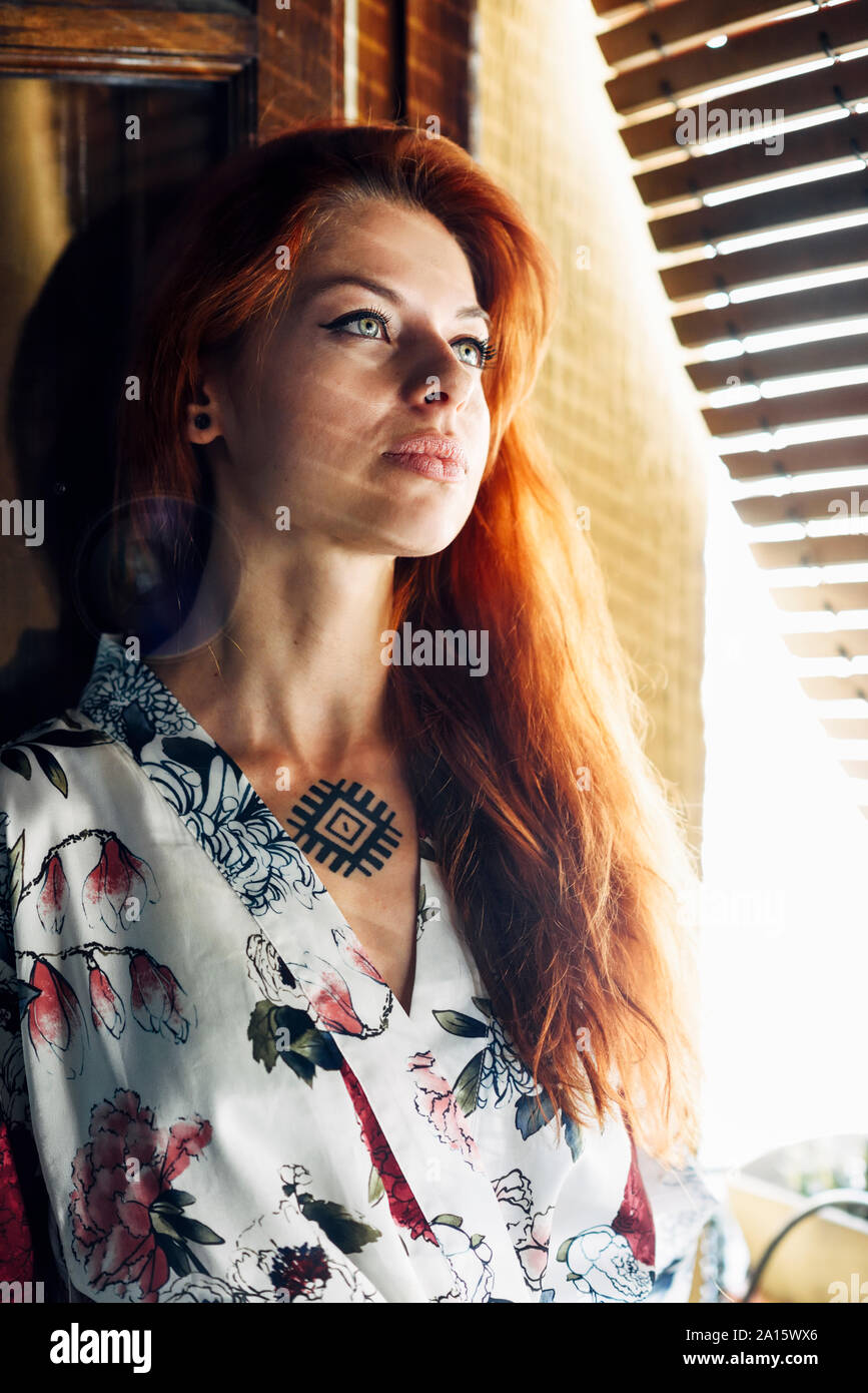 Portrait Of Red Haired Tattooed Woman At Home Looking Out Of Window