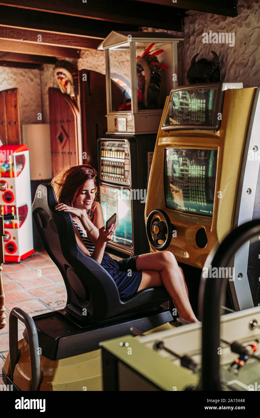 Young woman using cell phone in a driving simulator in a sports bar ...