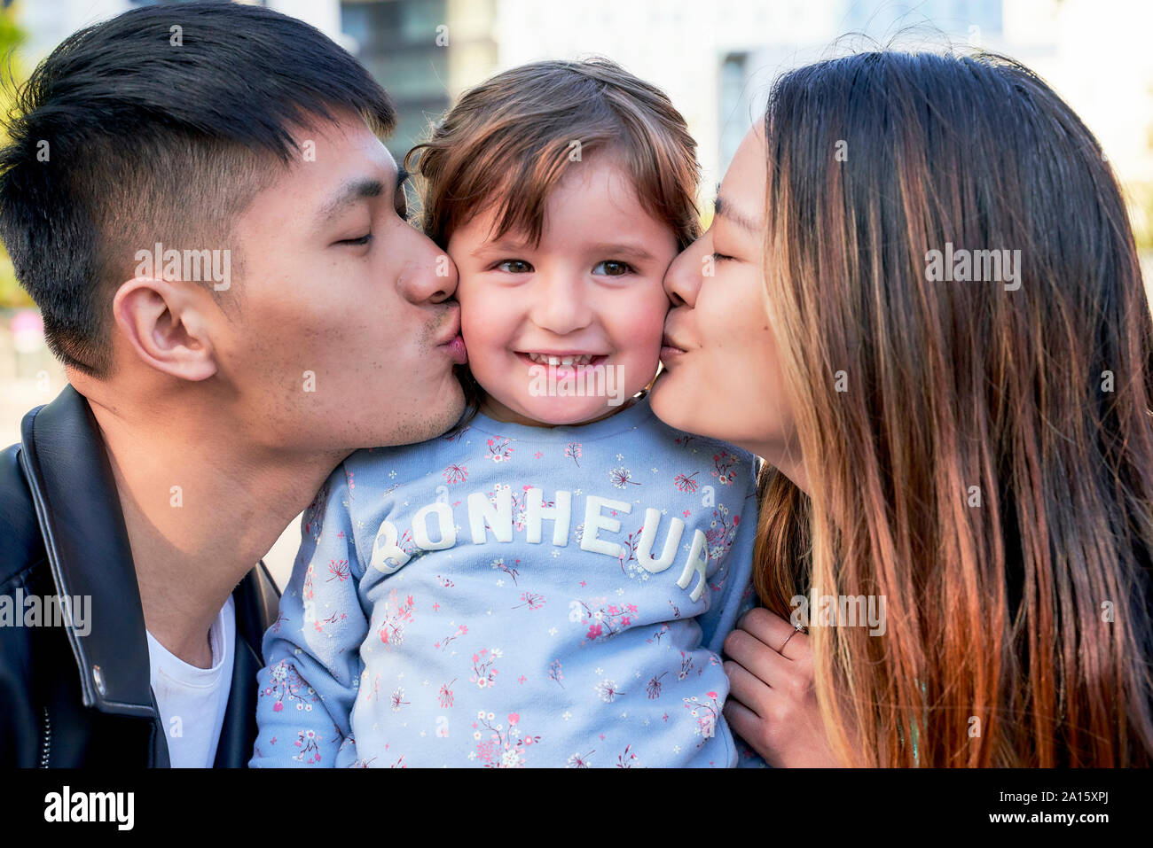 Happy parents kissing little girl Stock Photo - Alamy