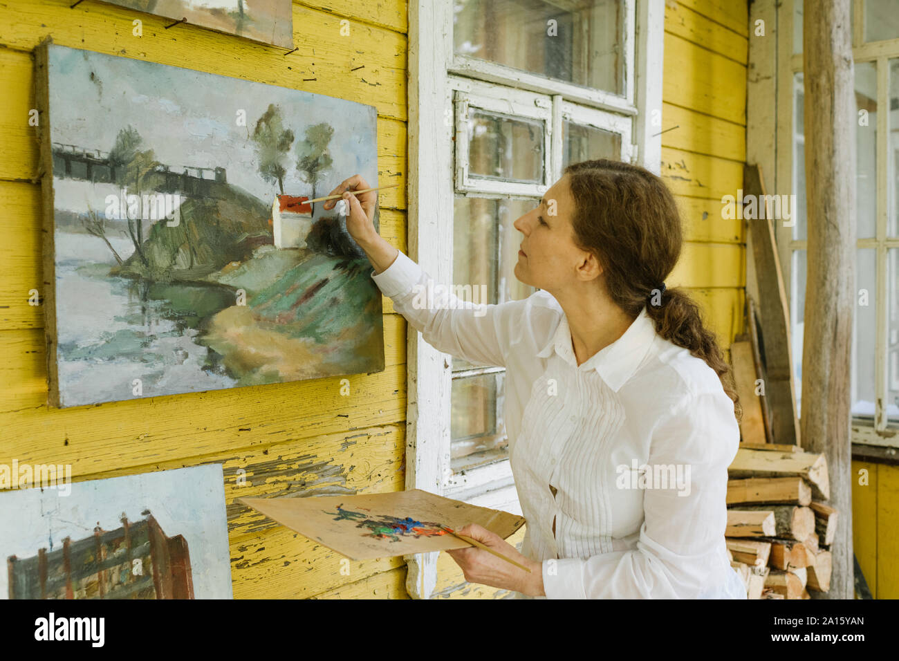 Female painter finishing her painting at old wooden village house ...