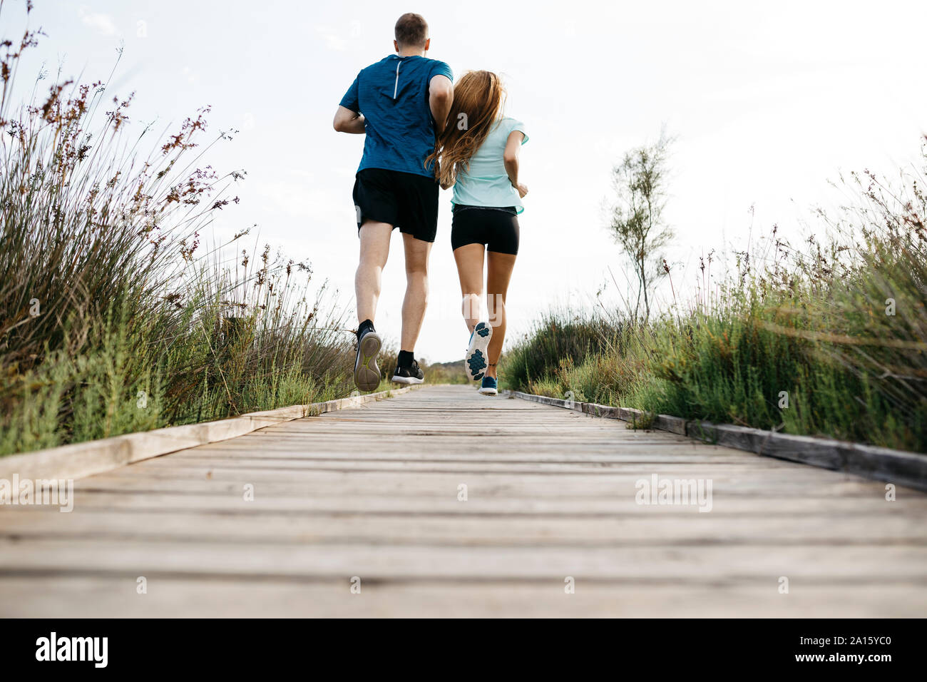 Rear view of young couple jogging on wooden walkway Stock Photo - Alamy