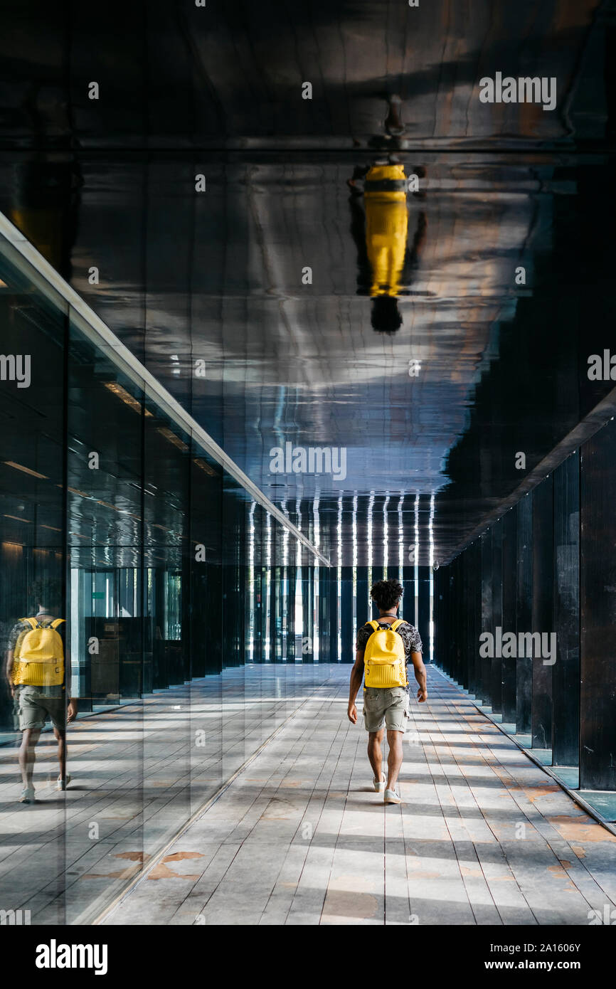 Back view of man with yellow backpack walking through a passage ...