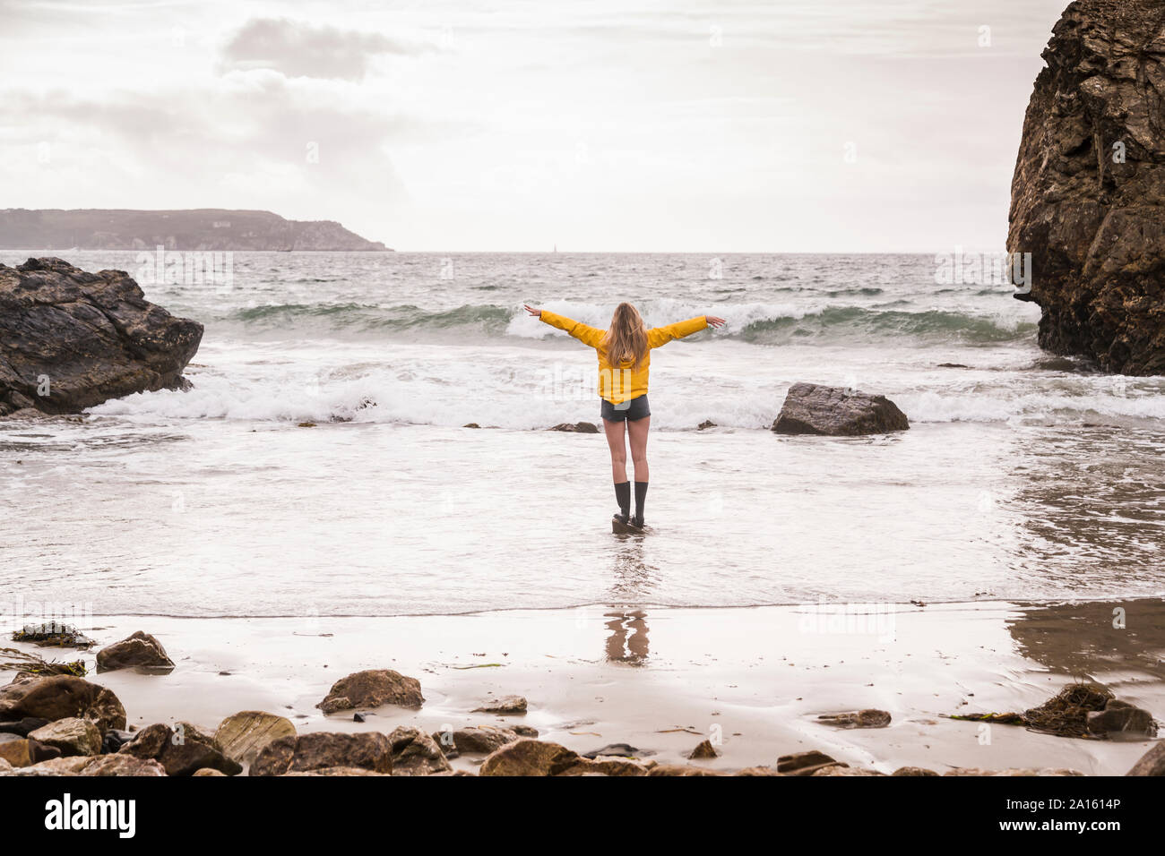 Rear view of young woman wearing yellow rain jacket with raised arms ...