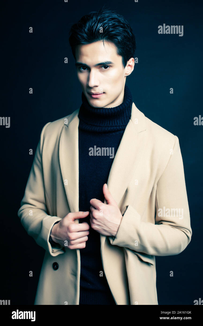 cool real young man in coat on black background posing, lifestyle ...