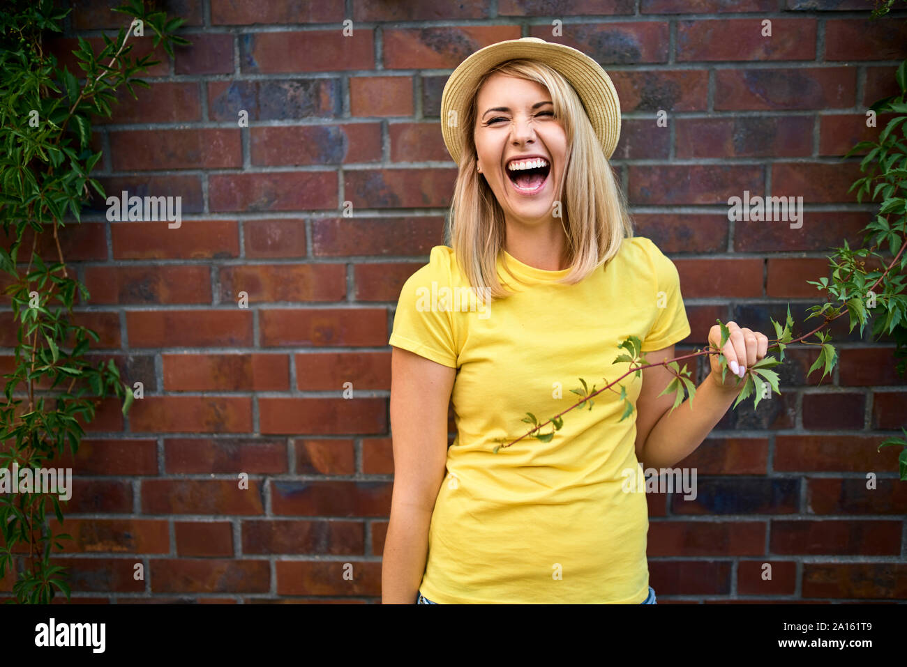 Portrait of laughing young woman standing at a brick wall Stock Photo ...