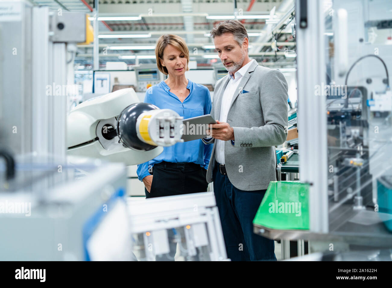 Businessman with tablet and woman talking at assembly robot in a ...