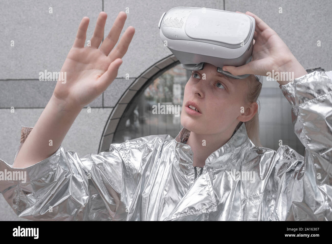 Girl in silver suit looking through VR goggles, watching her hand Stock ...