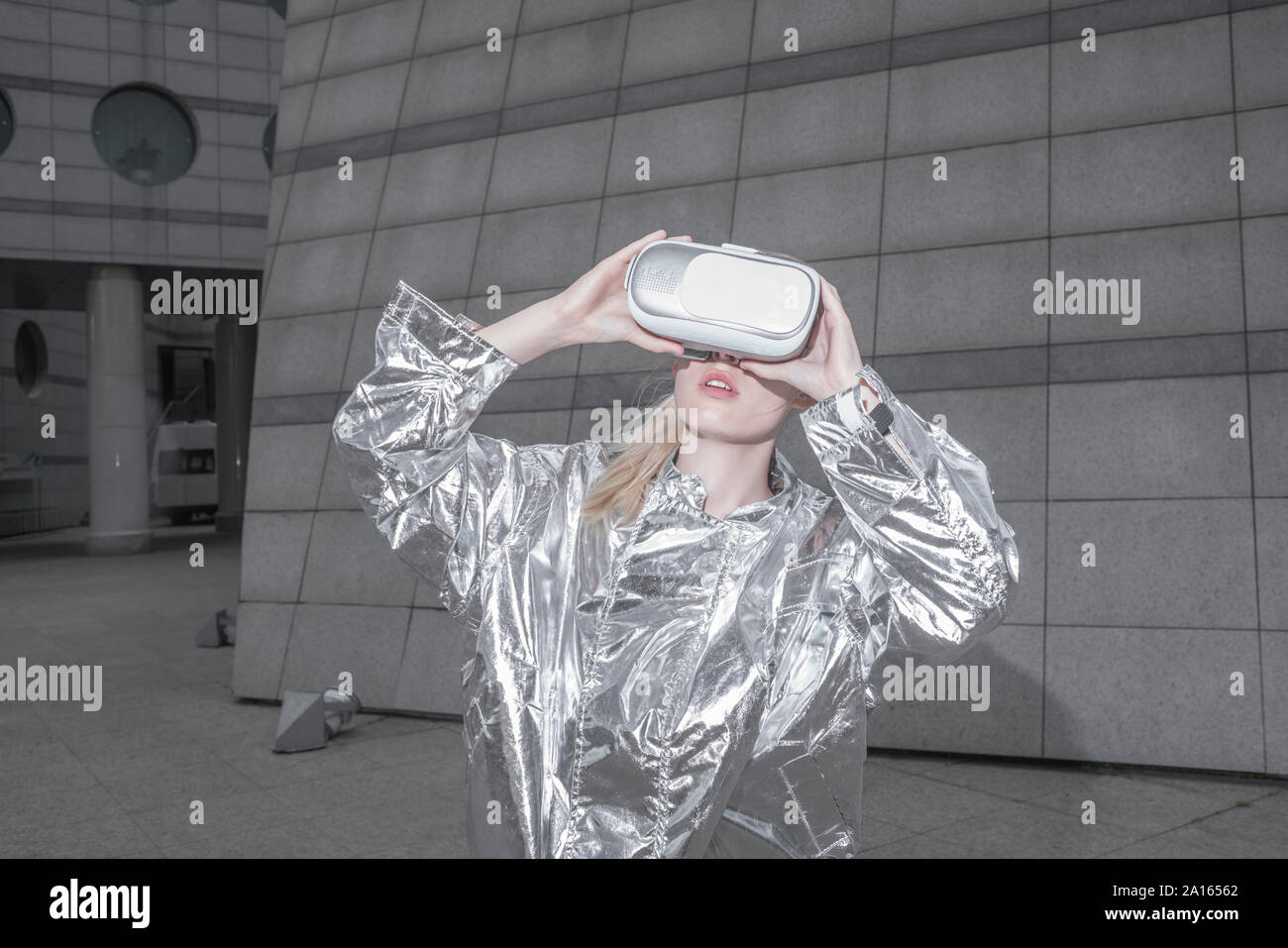 Girl in silver suit. looking through VR goggles in futuristic city ...