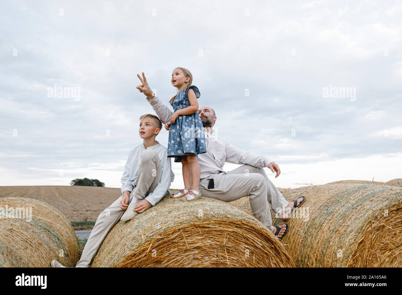 Father and his children sitting on hay bales, watching sky Stock Photo ...