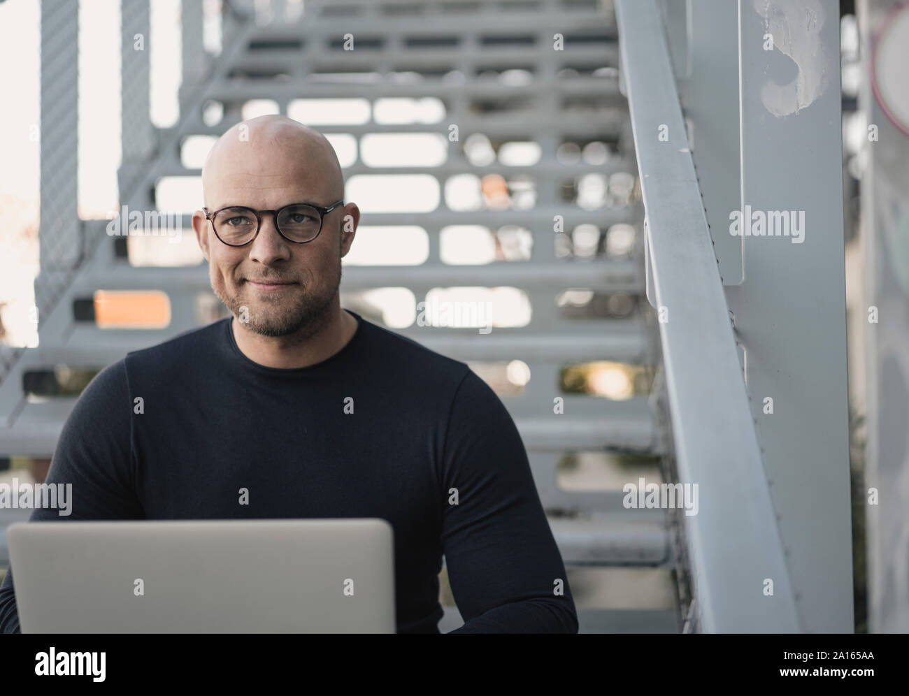 Portrait of bald man sitting on stairs using laptop Stock Photo - Alamy