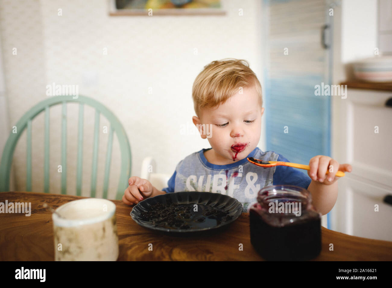 Cute little boy eating blueberry jam Stock Photo - Alamy