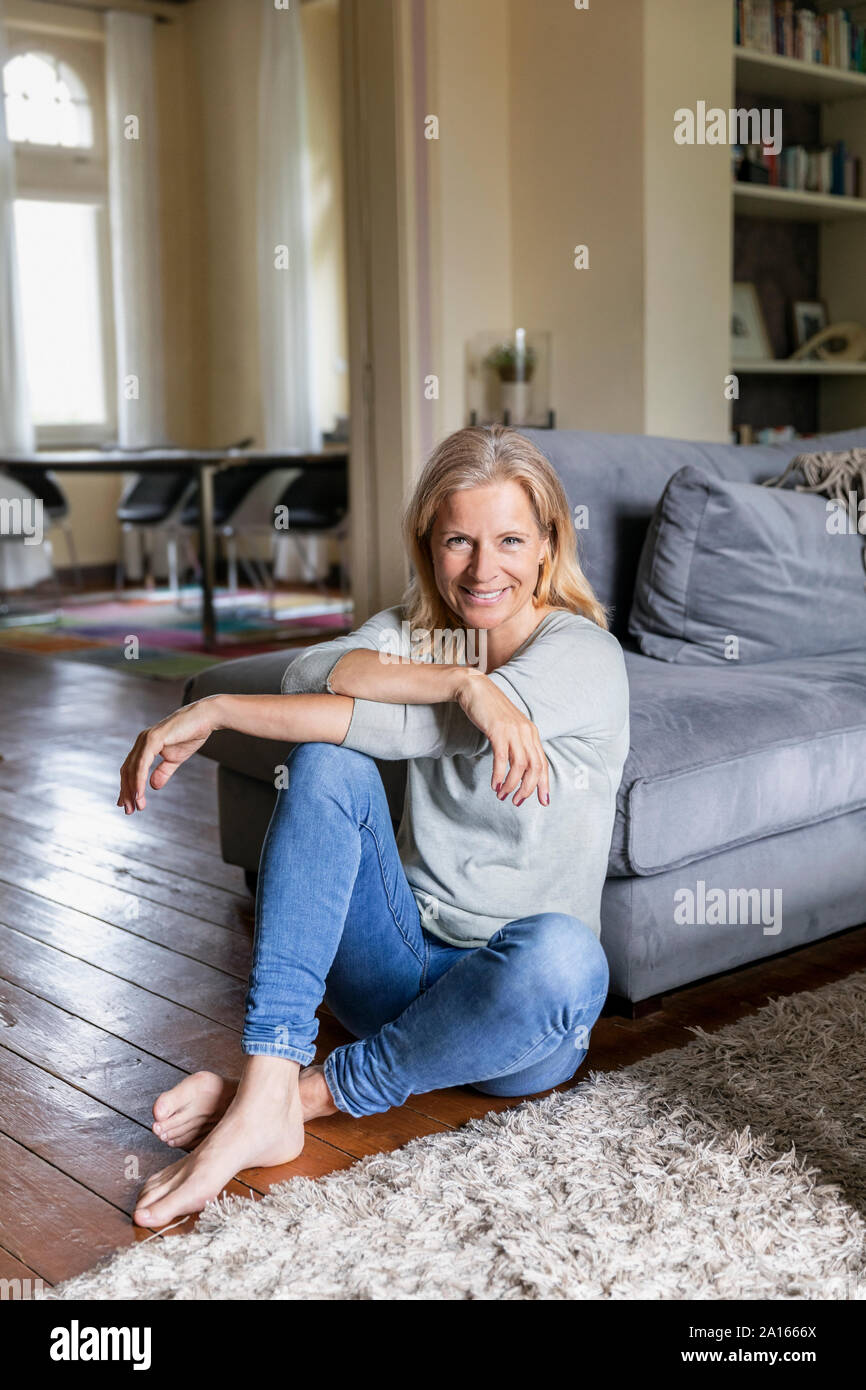 Portrait of smiling mature woman siiting barefoot on the floor in the living room Stock Photo ...