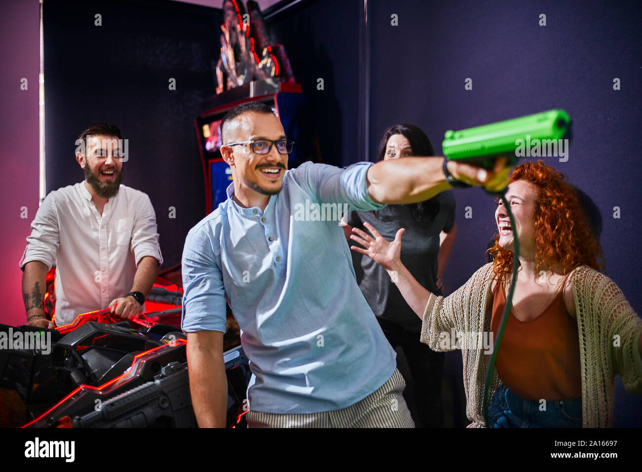 Happy friends playing and shooting with pistols in an amusement arcade ...