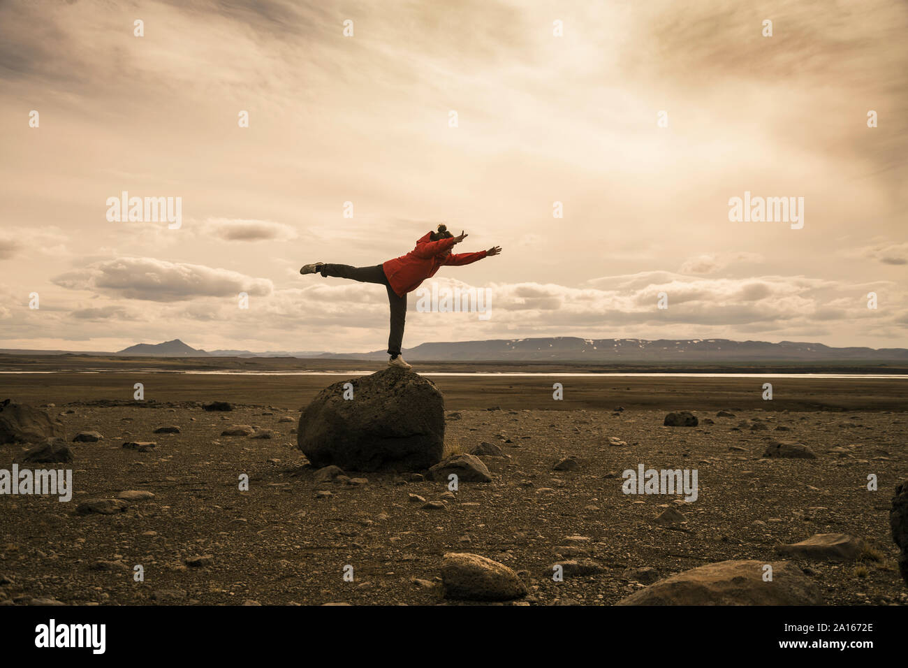 Young woman balancing on one leg on a rock in the volcanic highlands of ...