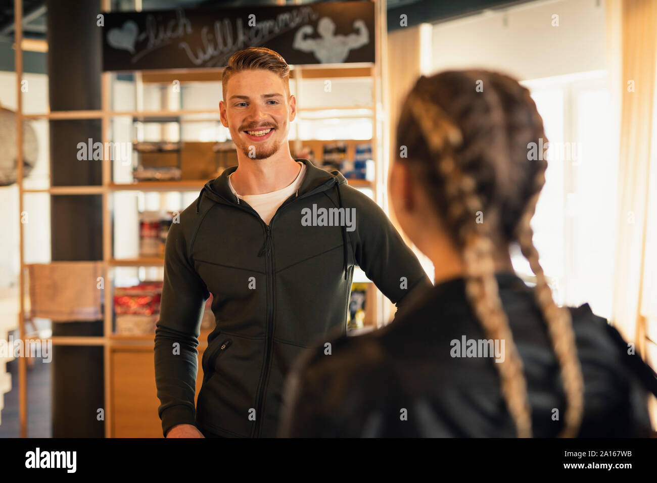 Coach talking to young woman at front desk of a gym Stock Photo - Alamy
