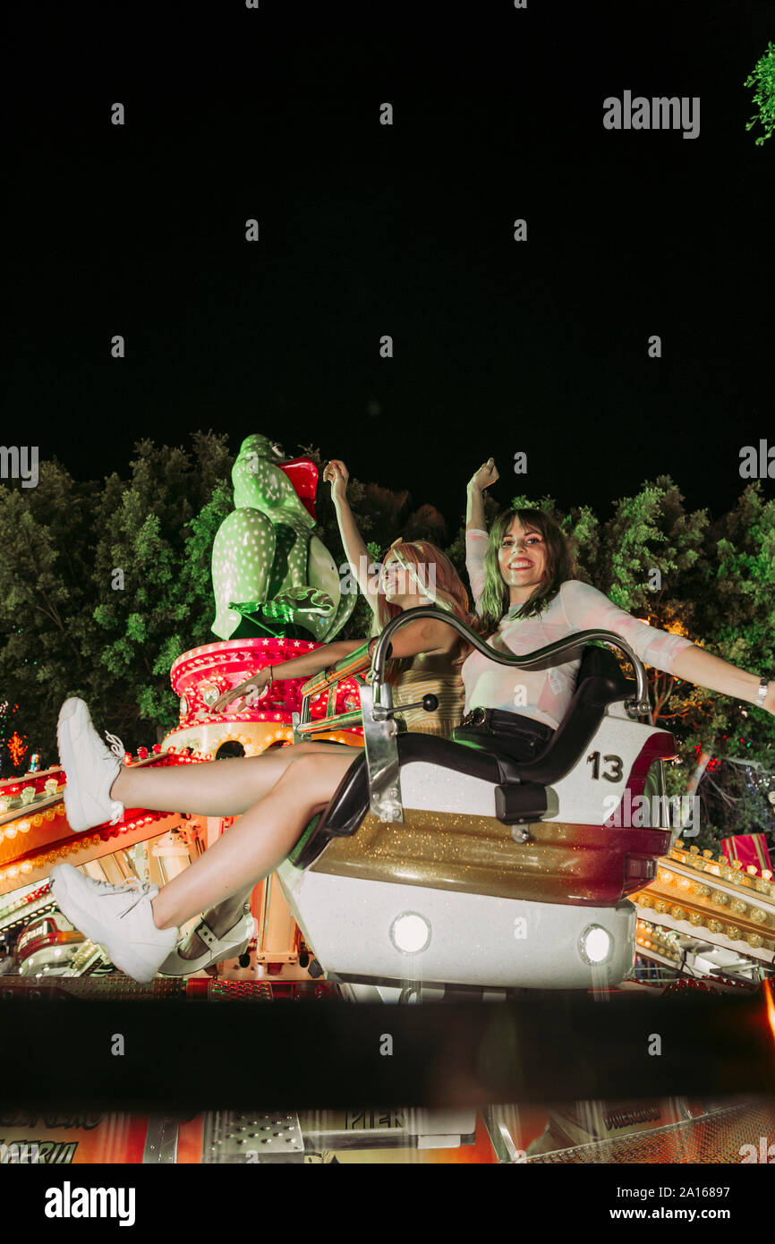 Two excited young women in a fairground ride on a funfair at night ...