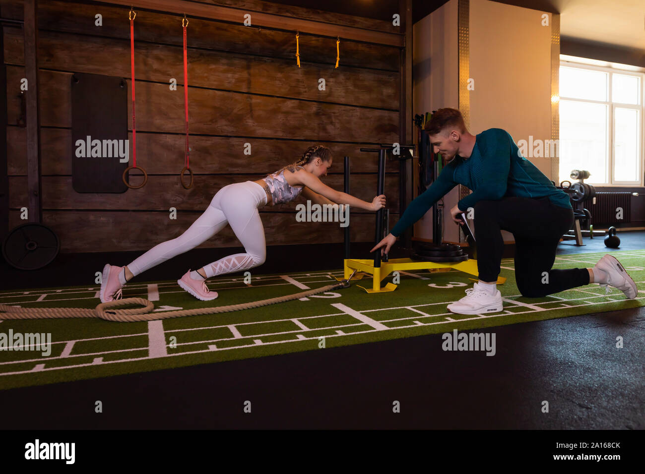 Young woman exercising in fitness gym with personal trainer pushing ...