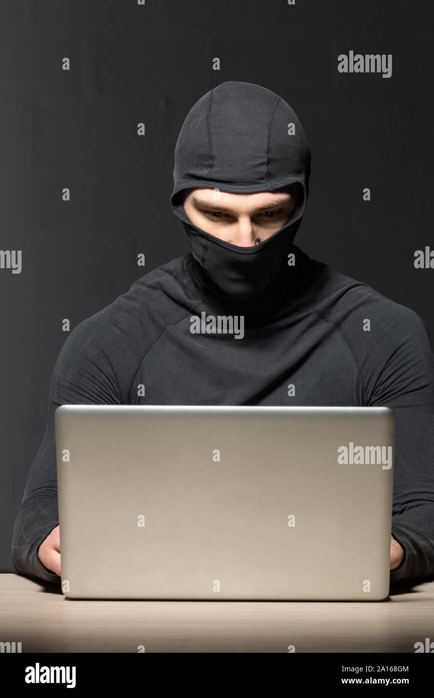 Masked hacker using laptop Stock Photo - Alamy