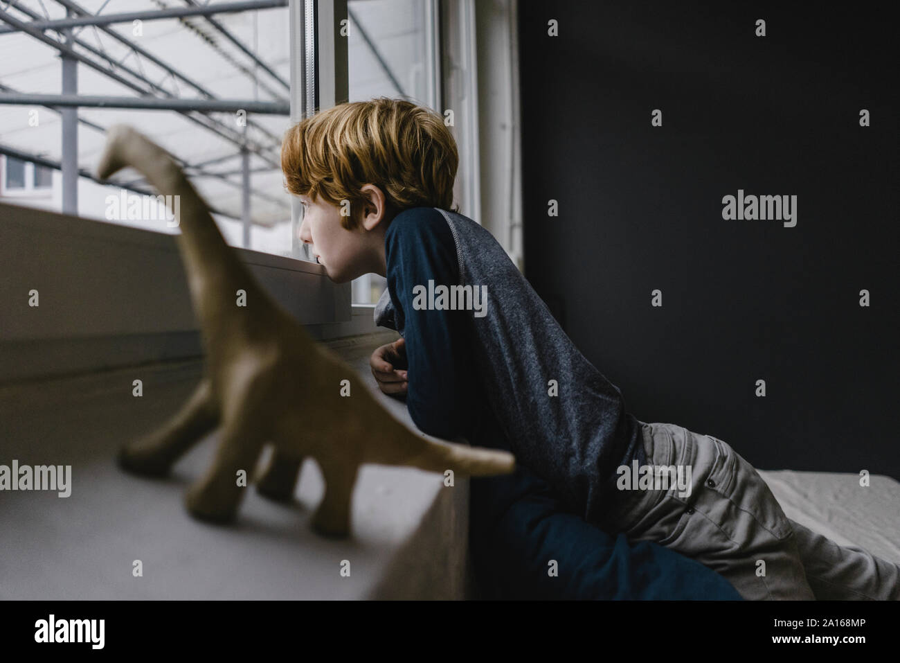 Sad boy leaning on window sill looking out of window in the evening ...