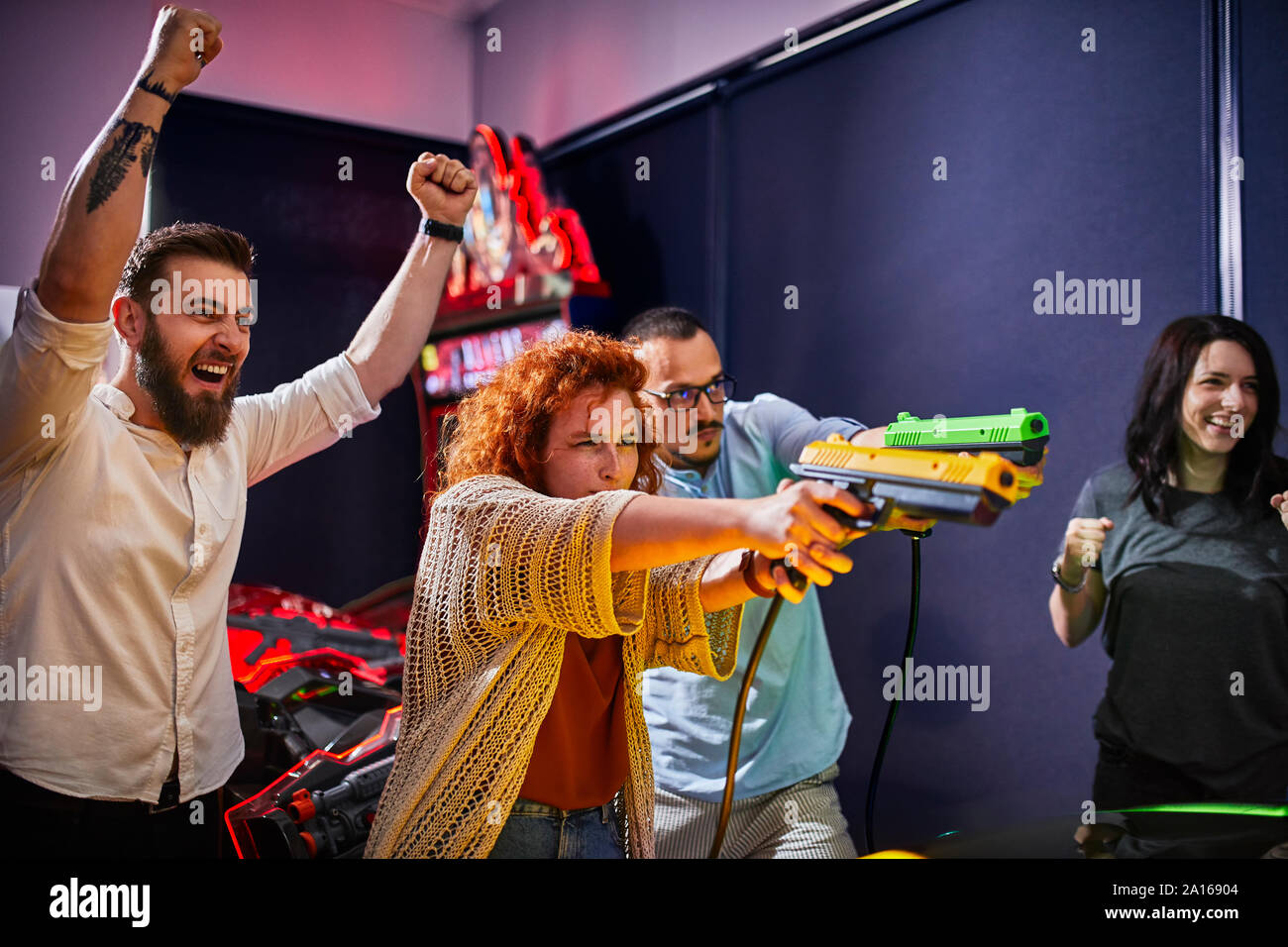 Happy friends playing and shooting with pistols in an amusement arcade ...