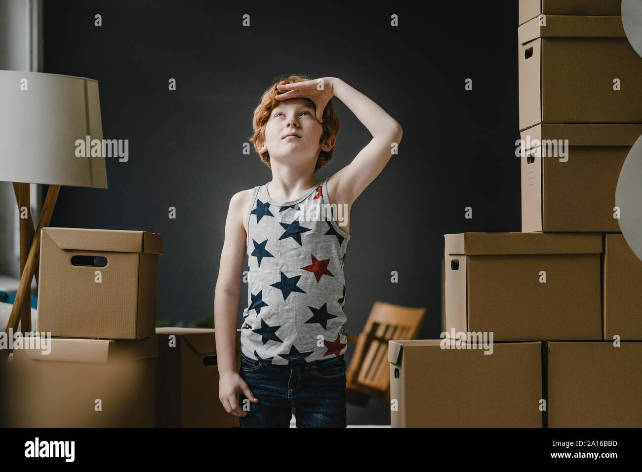 Portrait of redheaded boy standing beside cardboard boxes looking up ...